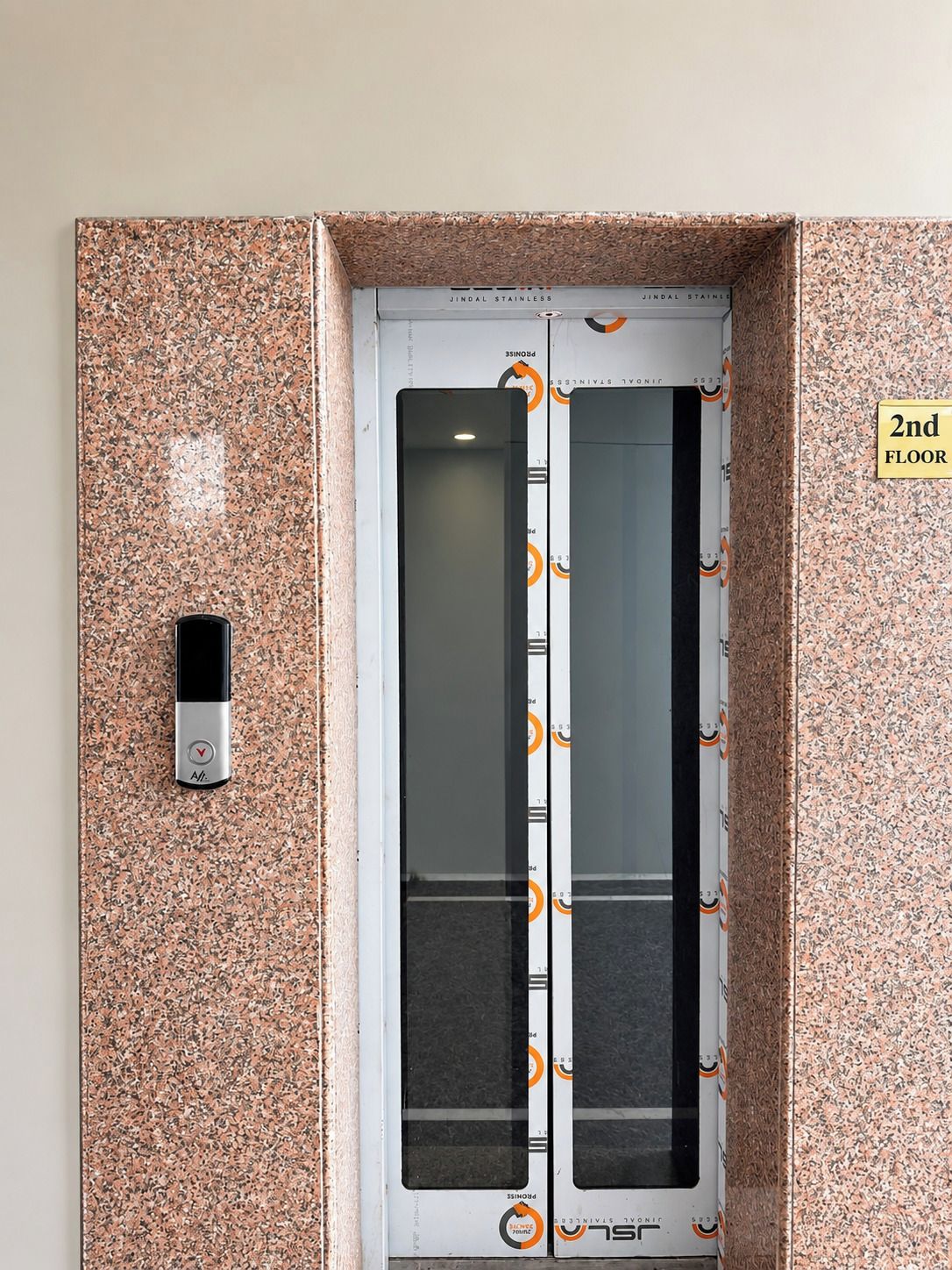 Um elevador com acabamento em aço inoxidável, painel de controle digital e placa indicando o 2º andar.