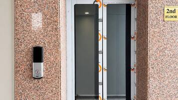Um elevador com acabamento em aço inoxidável, painel de controle digital e placa indicando o 2º andar.
