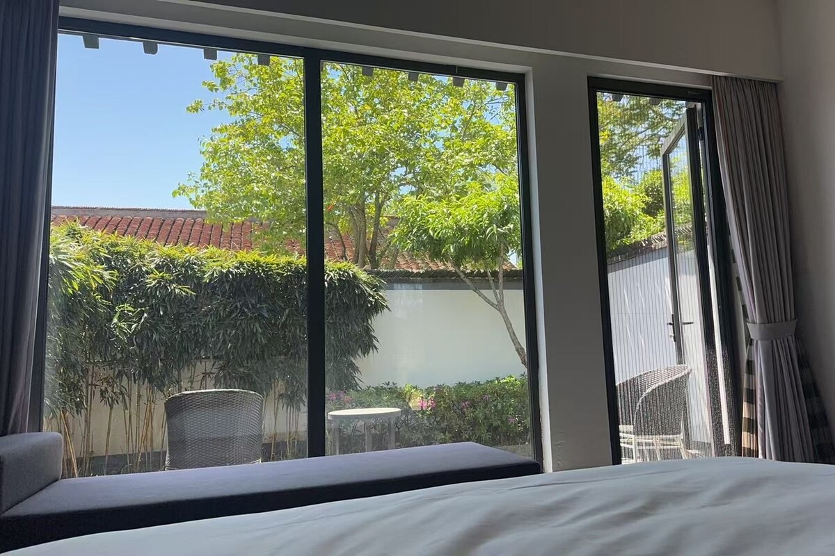 Quarto de hotel com uma cama, vista para um jardim e porta de correr de vidro.