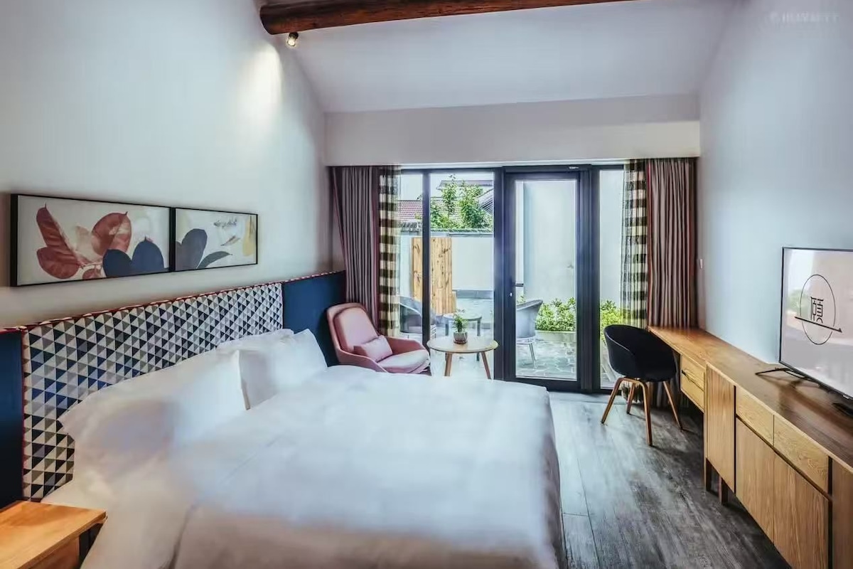 Quarto de hotel com cama grande, escrivaninha, cadeira e vista para o exterior.
