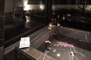 Um banheiro com piso de mármore, banheira, toalha e pétalas de rosa no chão.