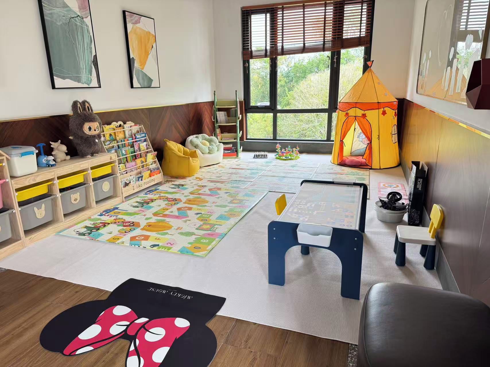 Um quarto de brincar infantil com uma janela grande, uma tenda de jogos e um tapete com letras do alfabeto.