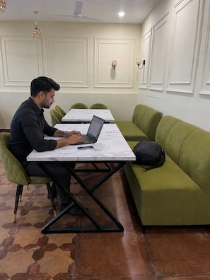 Um homem trabalhando em uma mesa com um laptop, um sofá verde e um chão de azulejos.