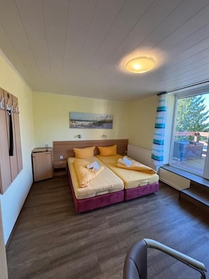 Um quarto com cama, mesa de cabeceira, janela com cortinas e uma cadeira.