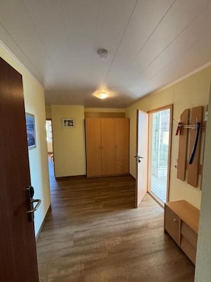 Um corredor com piso de madeira, uma porta à esquerda e um banco à direita.