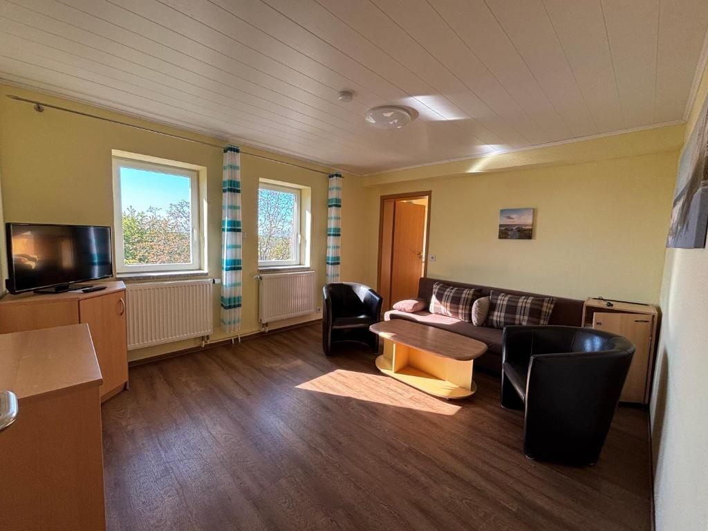 Sala de estar com sofá, cadeiras, mesa de centro, televisão e janela com cortinas.