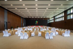 Uma grande sala de conferências com mesas redondas, cadeiras brancas e um palco com um logotipo.