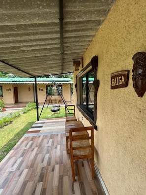 Área externa com banco de madeira e mesa, um letreiro com a inscrição 'BAIGA', e vista de um edifício ao fundo.