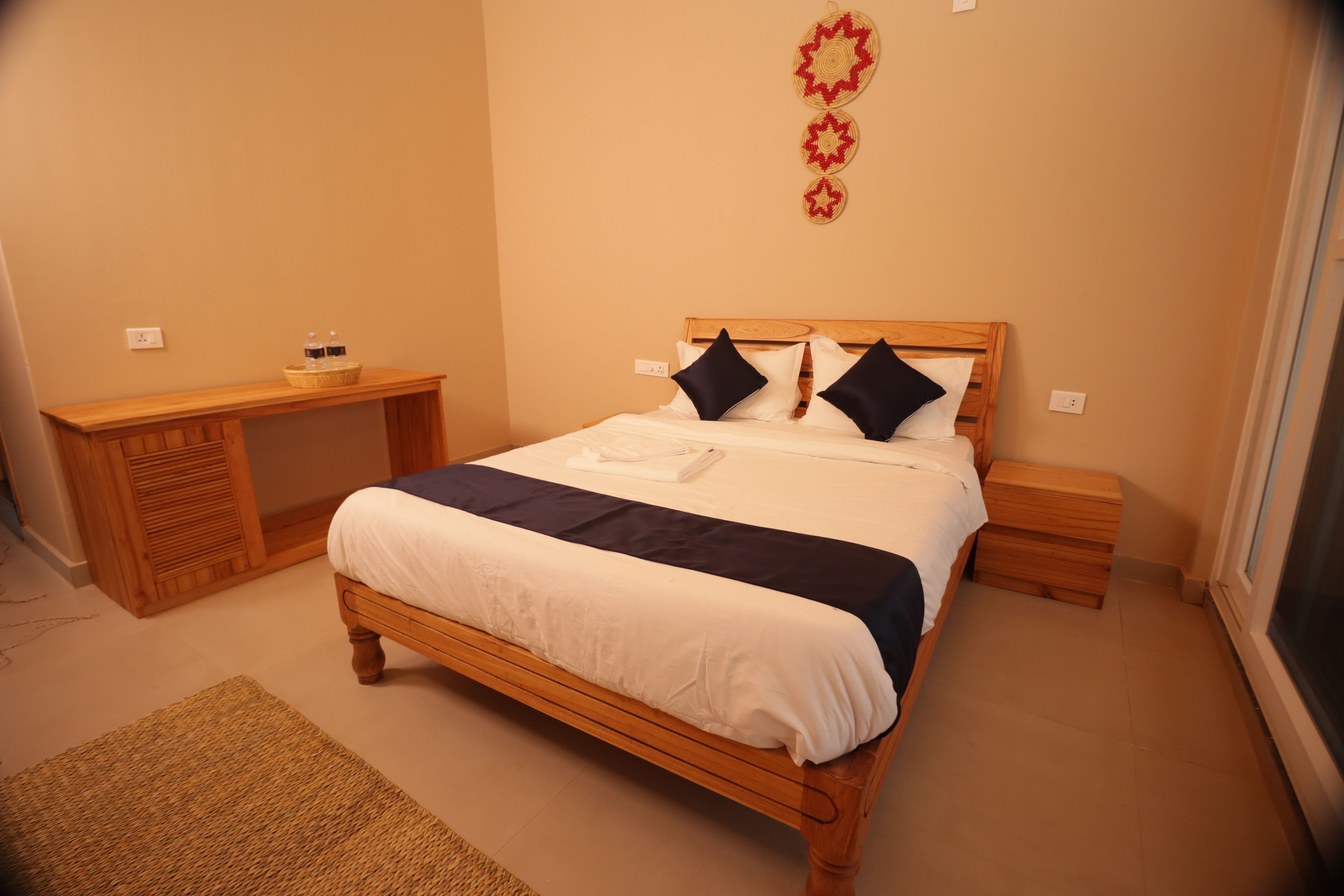 Quarto com cama de madeira, mesas de cabeceira, escrivaninha e objeto decorativo na parede.