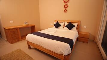 Quarto com cama de madeira, mesas de cabeceira, escrivaninha e objeto decorativo na parede.