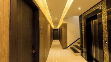 Um corredor moderno de hotel com portas de madeira, uma escadaria e um elevador.