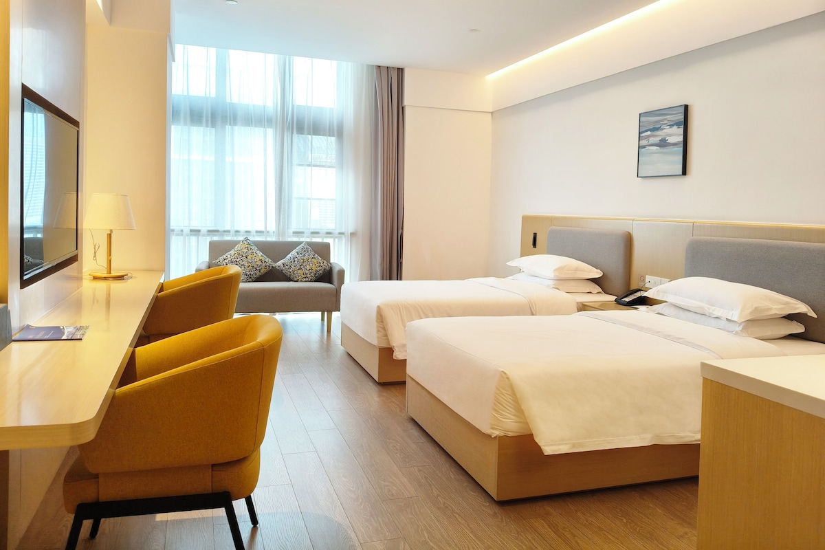 Quarto de hotel com cama, mesa de cabeceira, cadeira e escrivaninha com luminária.