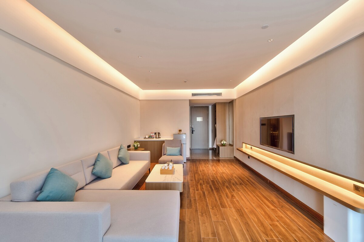 Quarto de hotel moderno com sofá, mesa de centro e televisão fixada na parede.