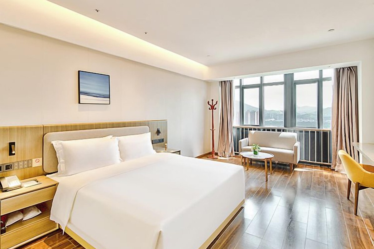 Quarto de hotel com uma cama grande, mesa de cabeceira, abajur e vista para a cidade pela janela.