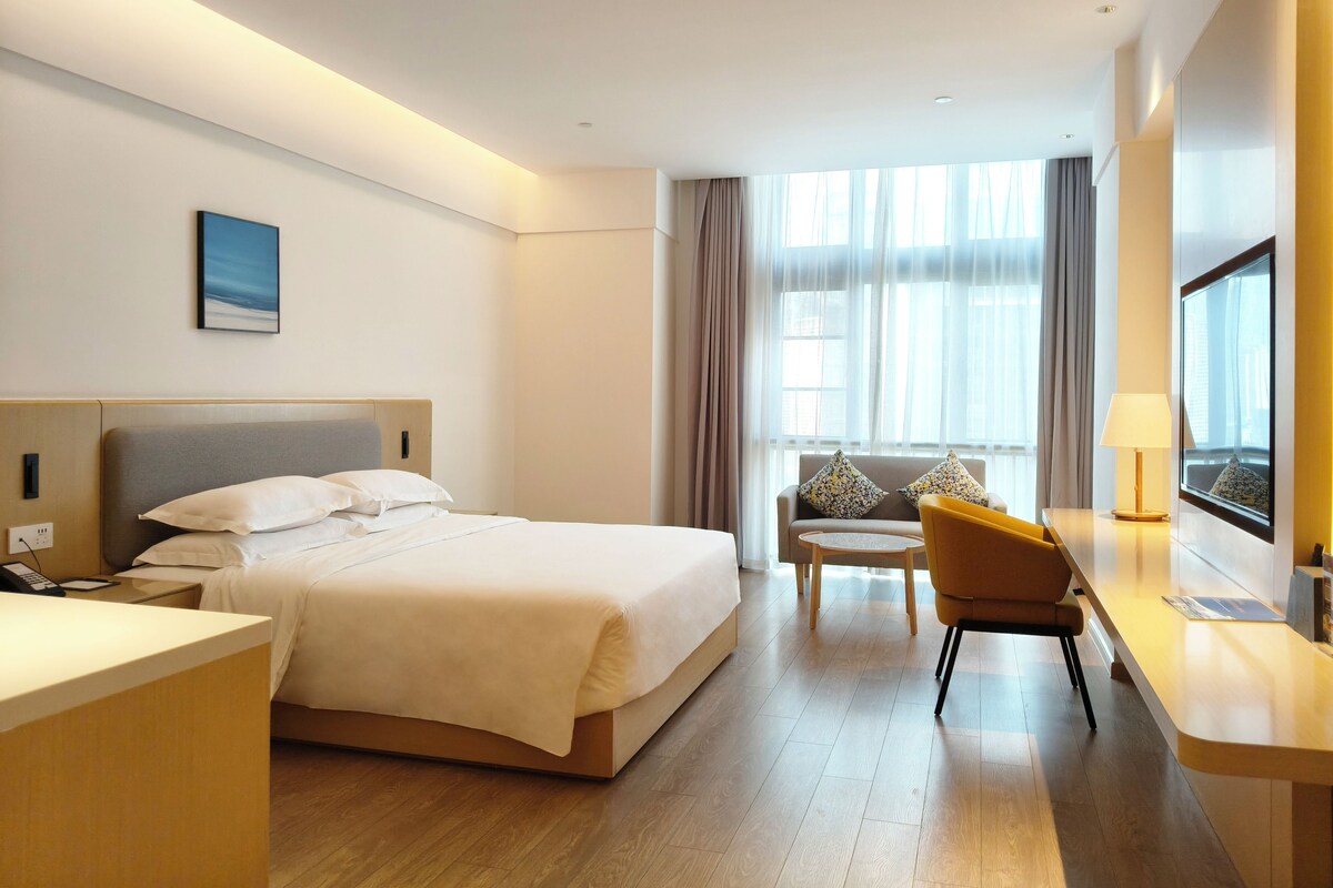 Quarto de hotel com cama, escrivaninha, cadeira e janela com cortinas.