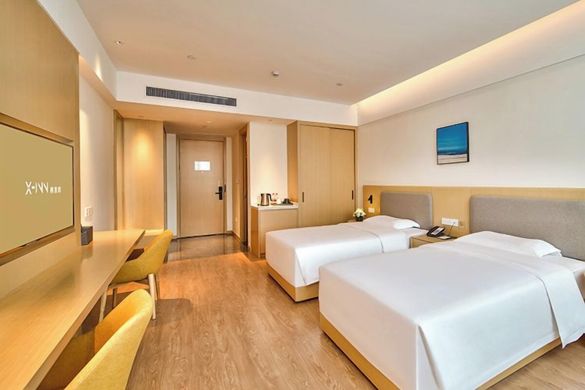 Quarto de hotel com duas camas, uma escrivaninha com cadeiras e uma televisão.