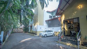Bairro residencial com um carro branco estacionado em frente a uma casa com escada de acesso à entrada.