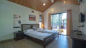 Quarto com cama de madeira, mesa de cabeceira, escrivaninha e uma janela grande com cortinas.