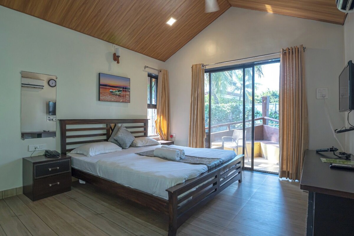 Quarto com cama de madeira, mesa de cabeceira, escrivaninha e uma janela grande com cortinas.
