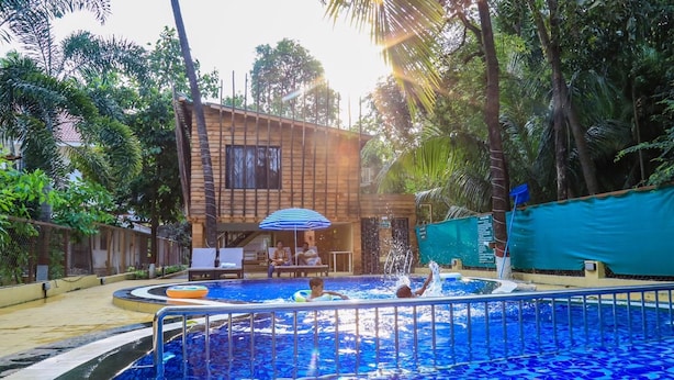 Área de piscina com um prédio de madeira, palmeiras e um espaço coberto para sentar.