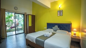 Quarto de hotel com cama, mesa de cabeceira, relógio de parede e porta de vidro corrediça para área externa.