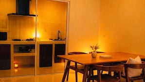 Sala moderna com área de refeições, um sofá e cozinha visível através de uma divisória de vidro.