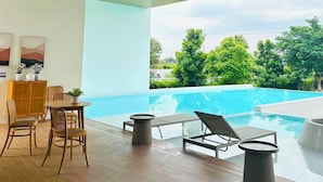 Uma área moderna de piscina interna com piso de madeira, espreguiçadeiras e uma mesa de jantar.
