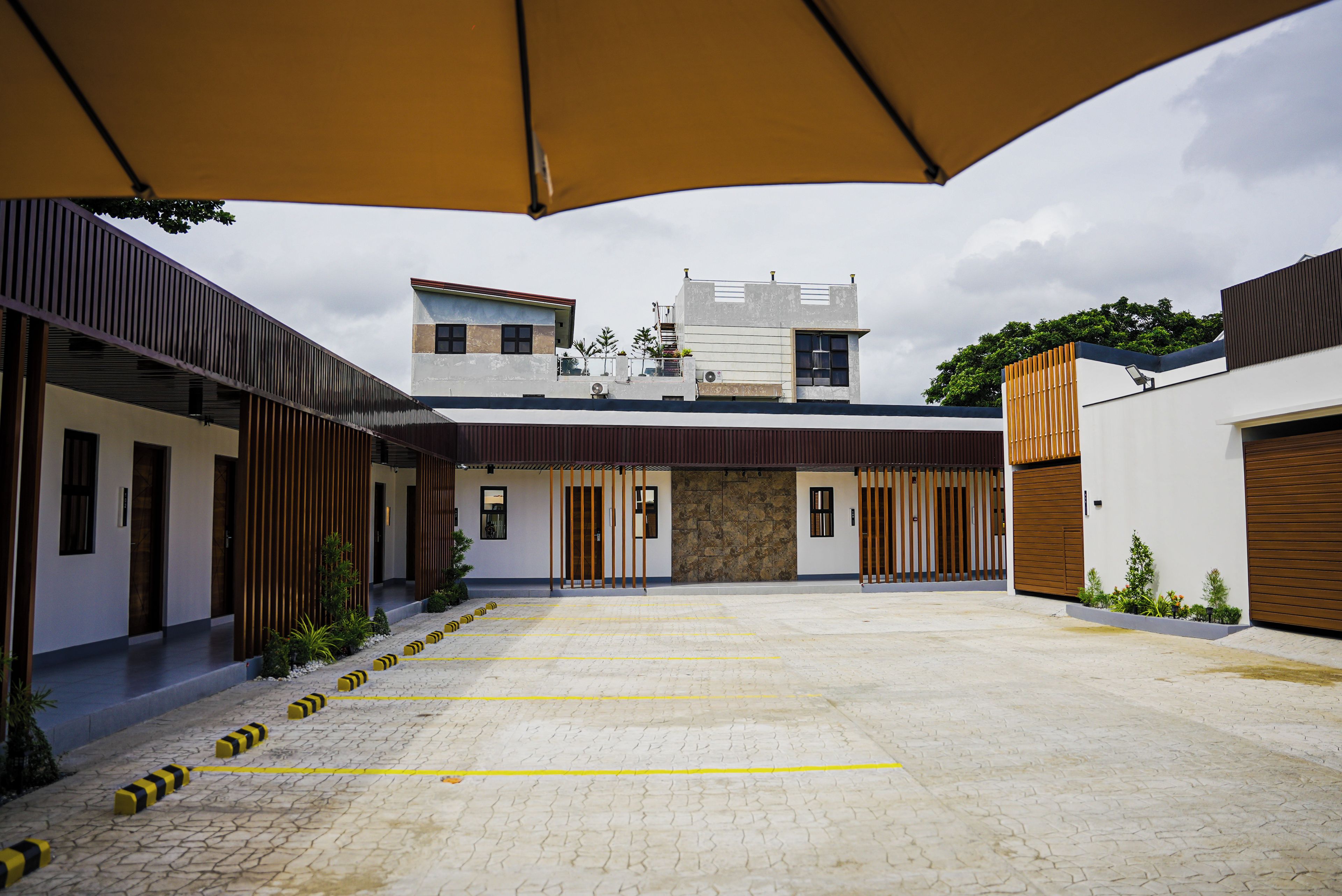 Um pátio com área de estar coberta, um caminho pavimentado e um edifício com várias portas e janelas.
