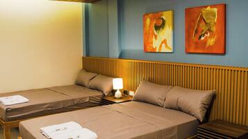 Quarto de hotel com duas camas, uma mesinha de cabeceira, um abajur e duas pinturas na parede.