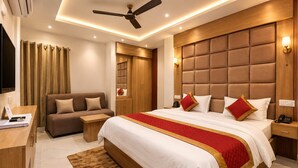 Quarto de hotel com cama grande, sofá, escrivaninha e ventoinha no teto.