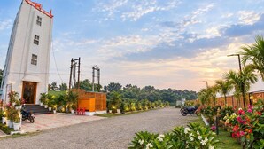 Um hotel com uma torre imponente, um caminho de entrada pavimentado e um jardim bem cuidado, com diversas plantas e flores.