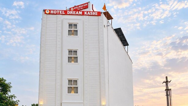 Hotel chamado 'Hotel Dream Kashi' com fachada branca, uma placa de identificação e uma escadaria que leva à entrada.