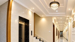 Corredor de hotel com piso de mármore, tapete vermelho, escada e lustre.