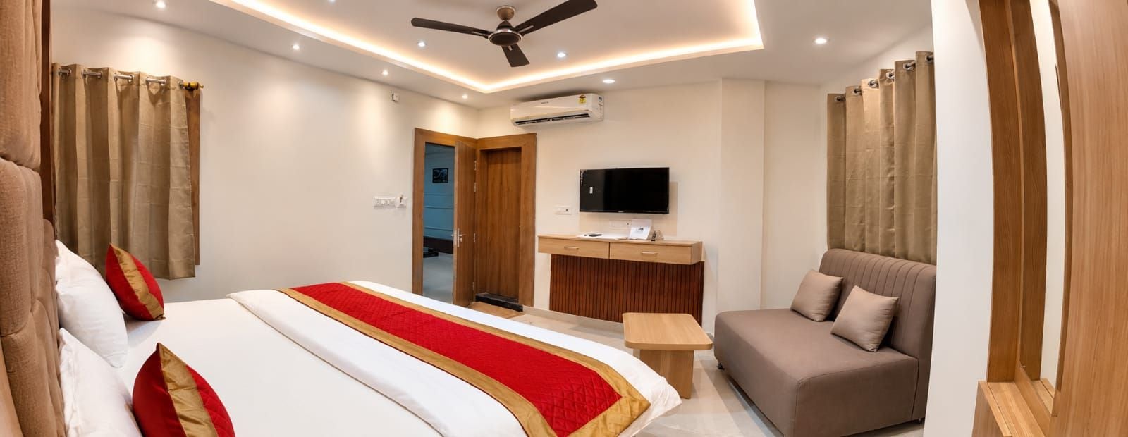 Quarto de hotel com cama, sofá, televisão e escrivaninha.