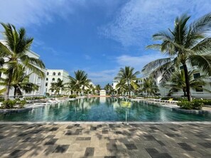 Área de piscina em resort, com palmeiras e céu claro.