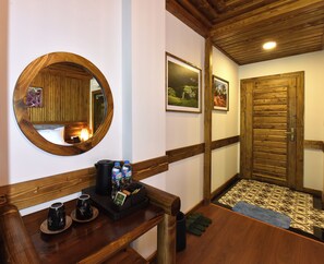 Quarto de hotel com espelho de moldura em madeira, espaço para café e porta com painel de madeira.