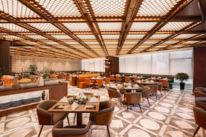 Restaurante com teto estampado, área de buffet e disposição de mesas e cadeiras.