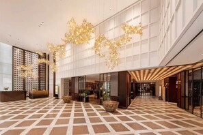 Um hall amplo com padrão de piso quadriculado, grandes janelas e luminárias decorativas.