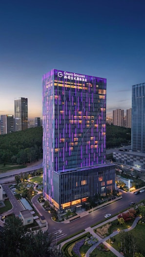 Um edifício moderno de arranha-céu com um design de iluminação vertical marcante, rodeado por um paisagismo urbano bem cuidado.