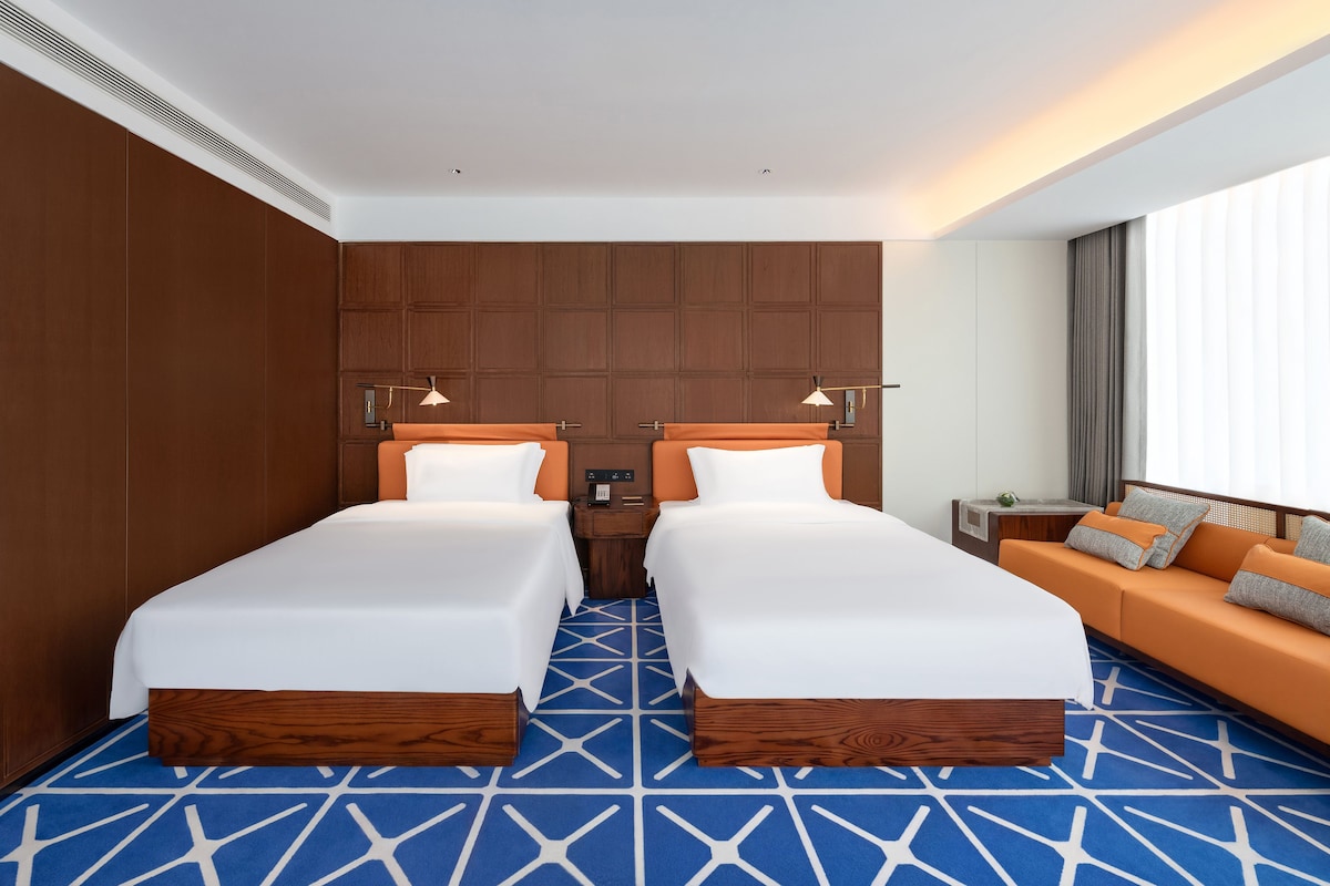 Quarto de hotel com duas camas, um sofá, uma mesinha e uma janela com cortinas.