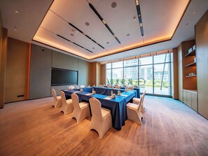 Uma sala de conferências com uma mesa comprida, cadeiras, uma TV de tela plana e amplas janelas que oferecem vista para prédios.