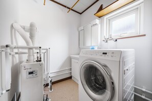 Uma lavanderia equipada com máquina de lavar de abertura frontal, secadora e sistema de ventilação.