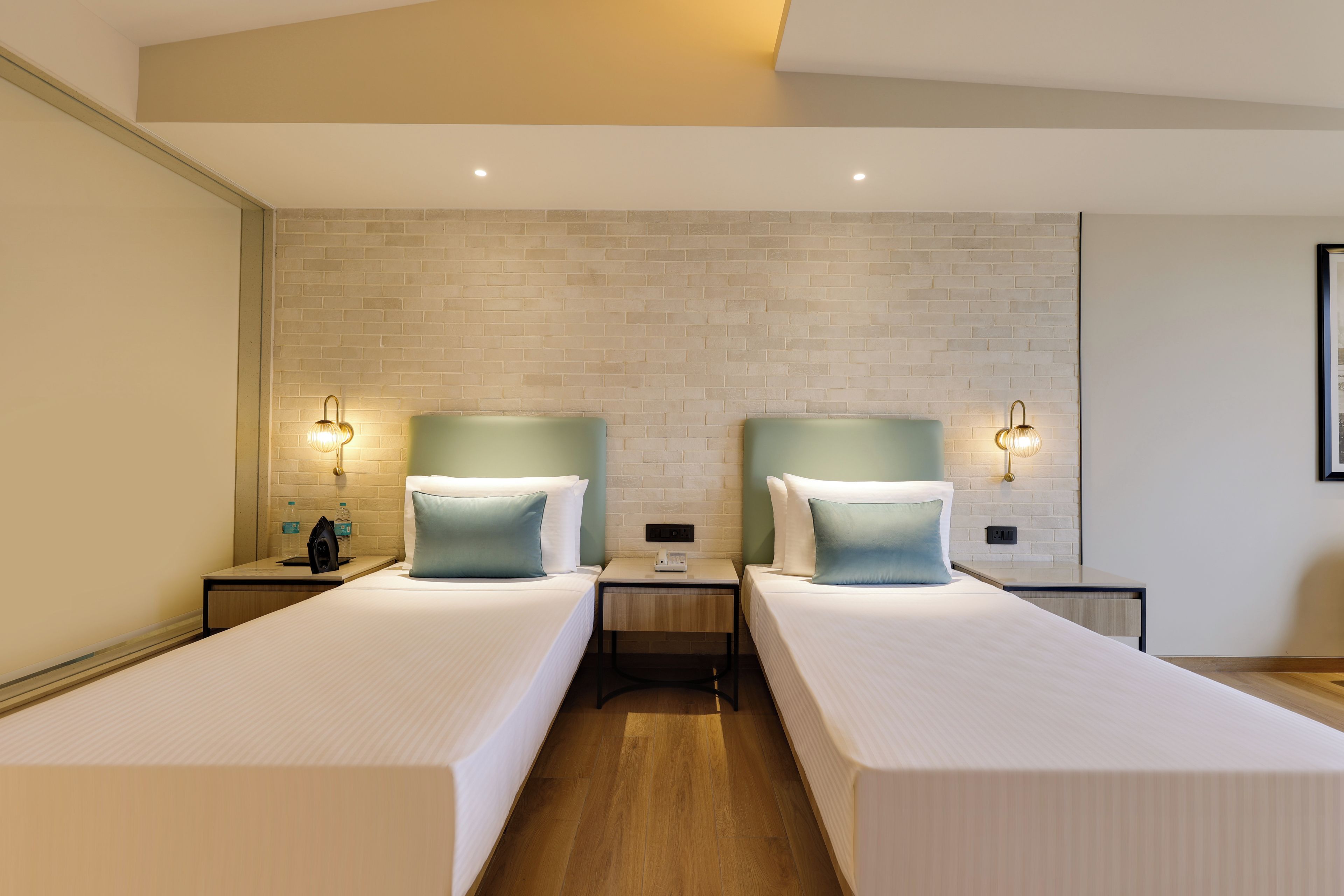 Quarto de hotel com duas camas de solteiro, parede de tijolos e luminárias modernas.