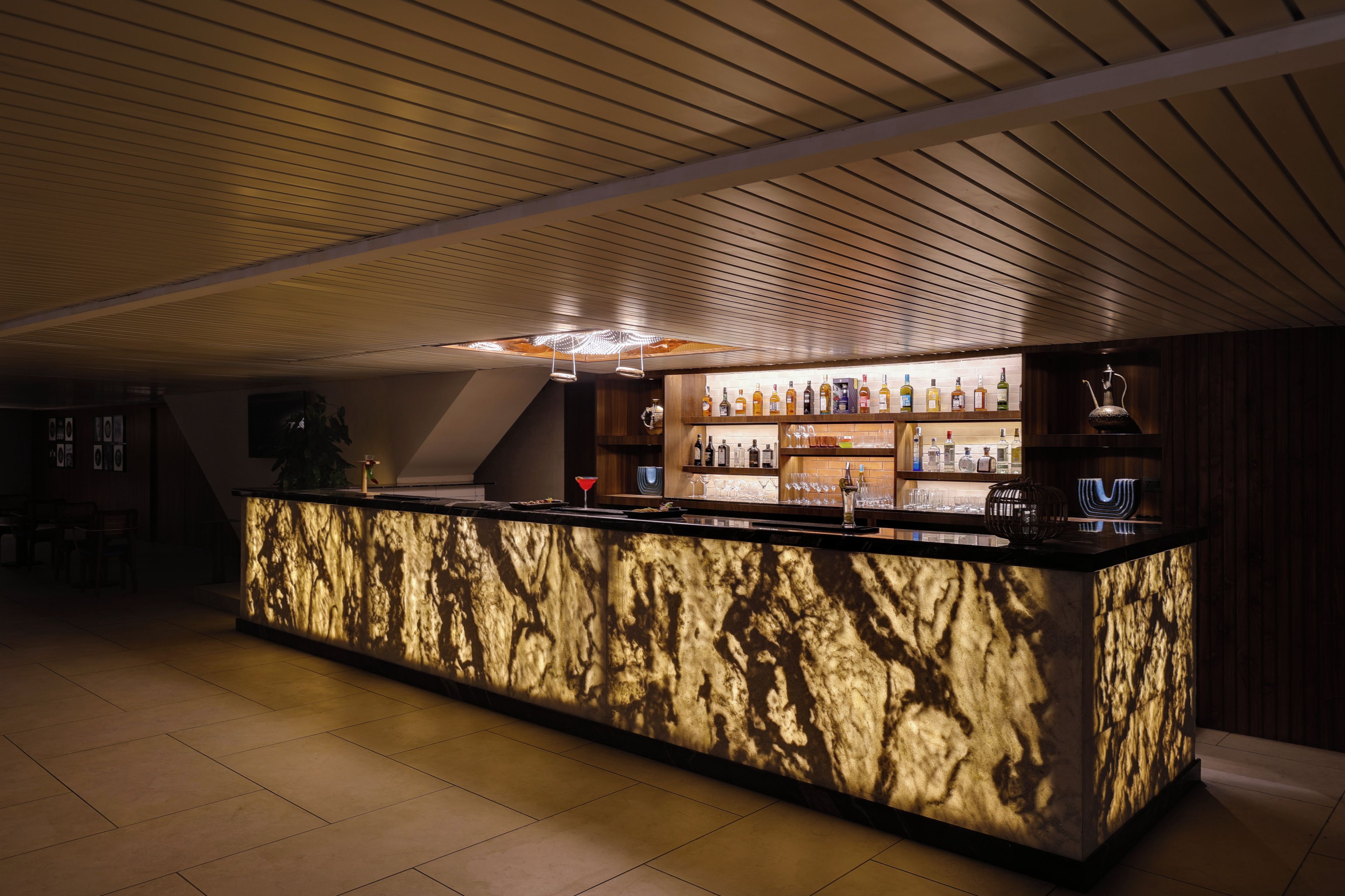 Uma área de bar com bancada de mármore, prateleiras cheias de garrafas e teto de madeira.
