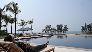 Área à beira da piscina com espreguiçadeiras, piscina e vista para o mar.