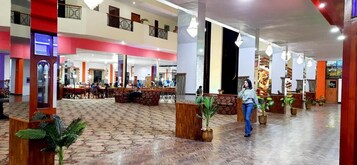Um hall amplo com piso estampado, diversas áreas de estar e um balcão de recepção central.