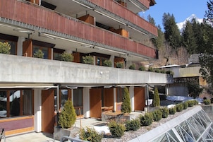 Hotel com vários andares, varandas, área de estar externa e vista para uma montanha.