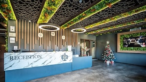 Uma área de recepção com balcão de mármore, ripas verticais de madeira, luminárias de teto circulares e um pinheiro de Natal.