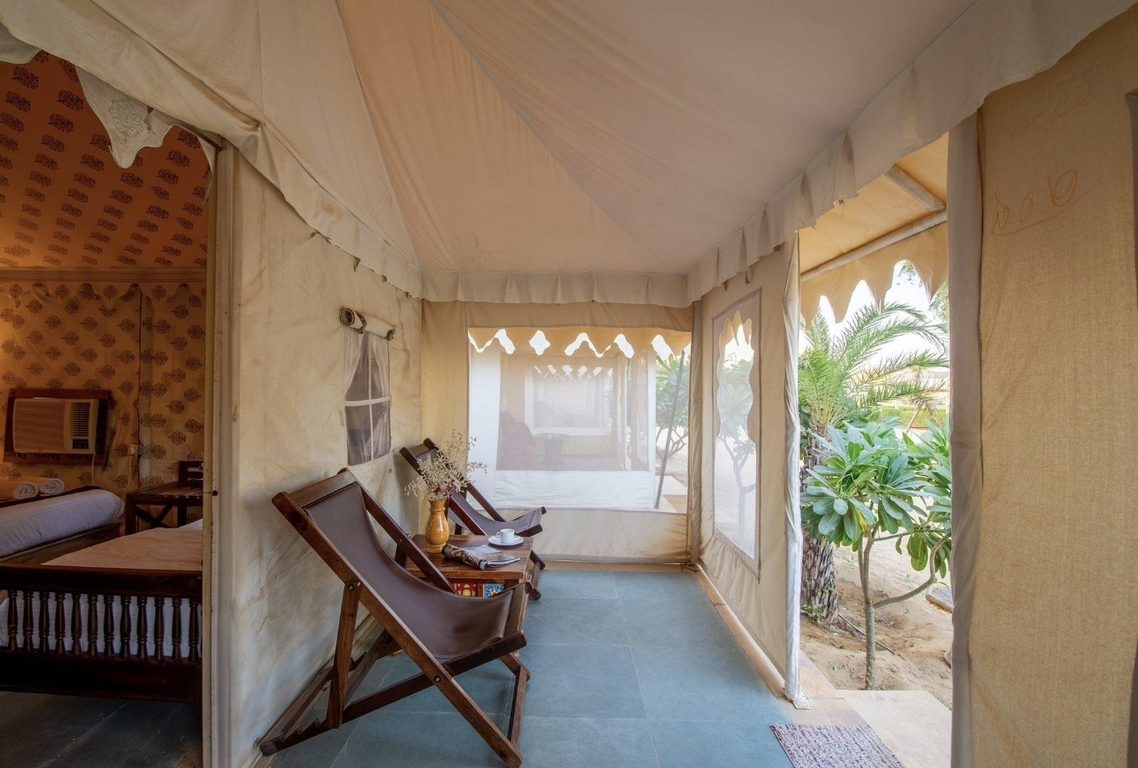 Quarto com tenda, uma cama, mesa com cadeiras e vista para o exterior.