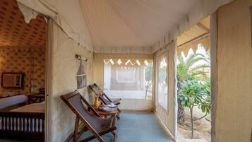 Quarto com tenda, uma cama, mesa com cadeiras e vista para o exterior.